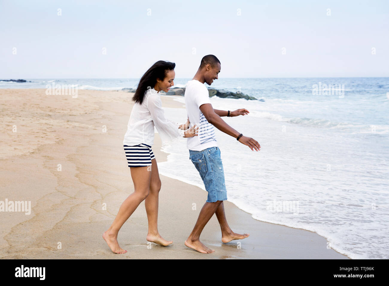 Woman pushing man while standing on shore at beach Stock Photo - Alamy