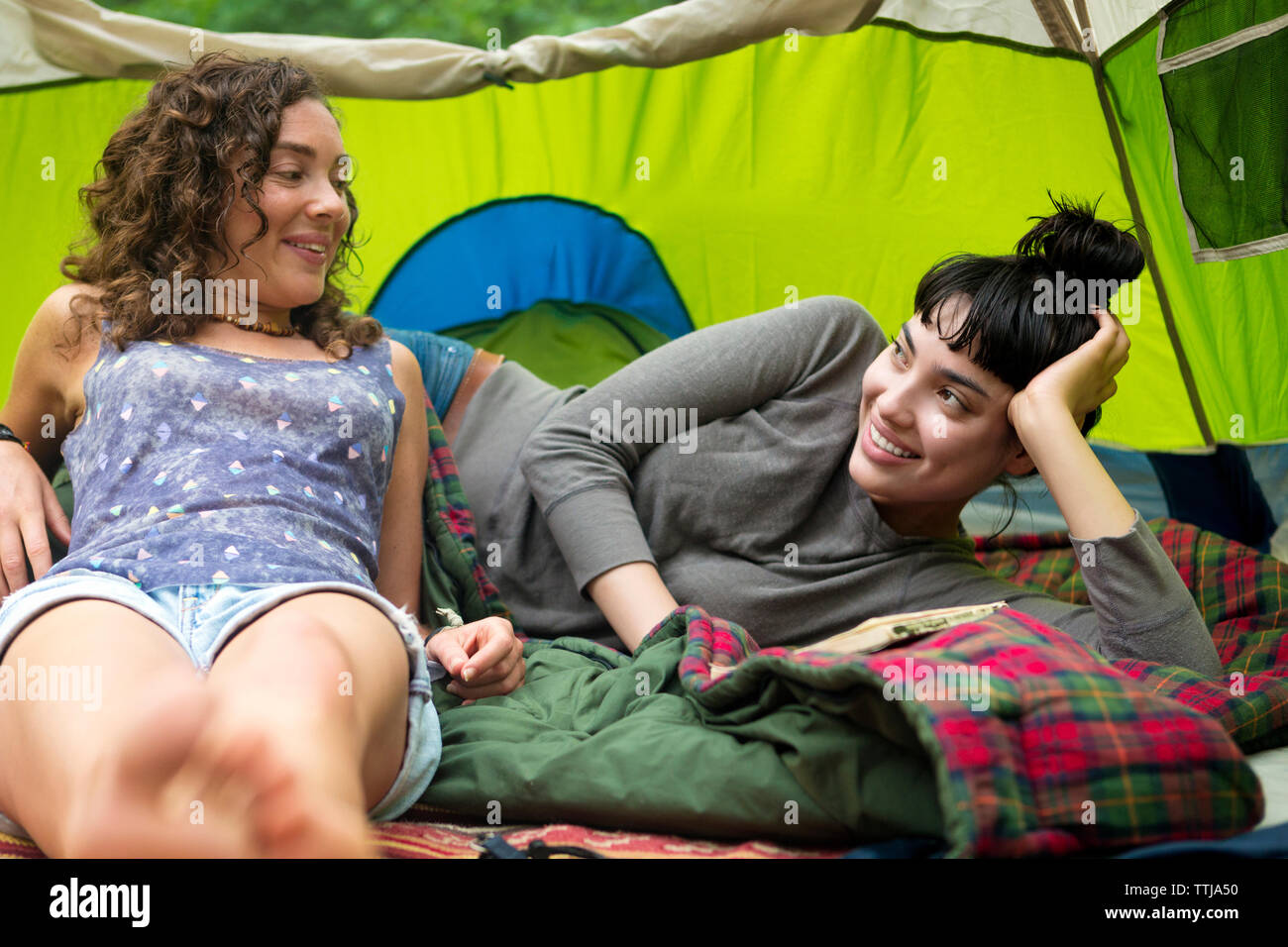 Happy friends relaxing on sleeping bag in tent Stock Photo - Alamy