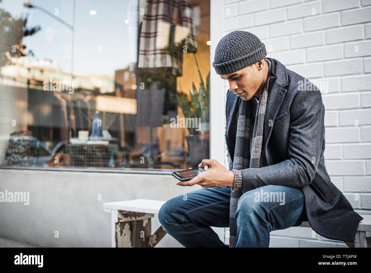 Man using mobile phone while sitting on bench against wall Stock Photo ...