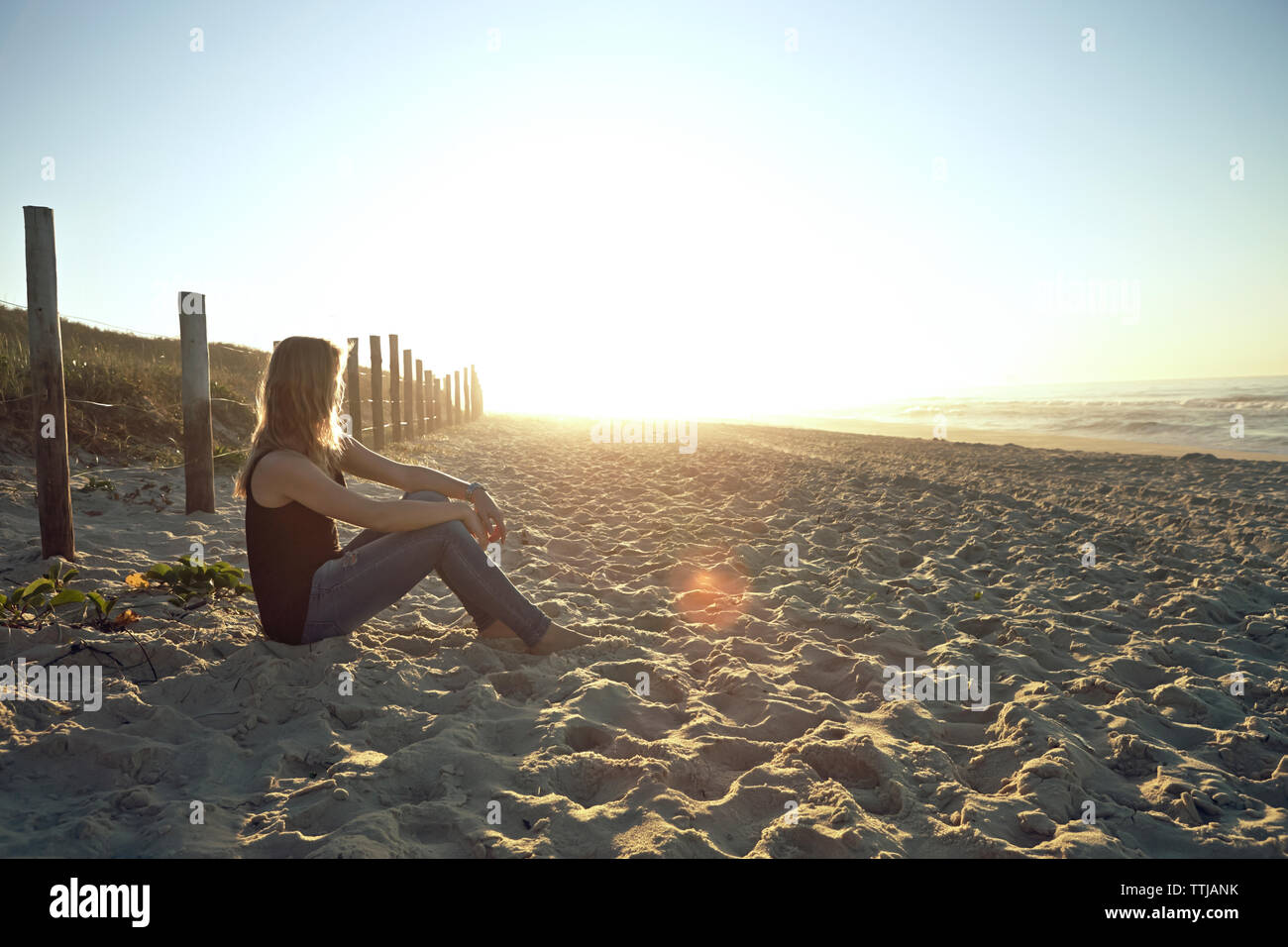Side view of woman sitting on sand at beach during sunset Stock Photo ...