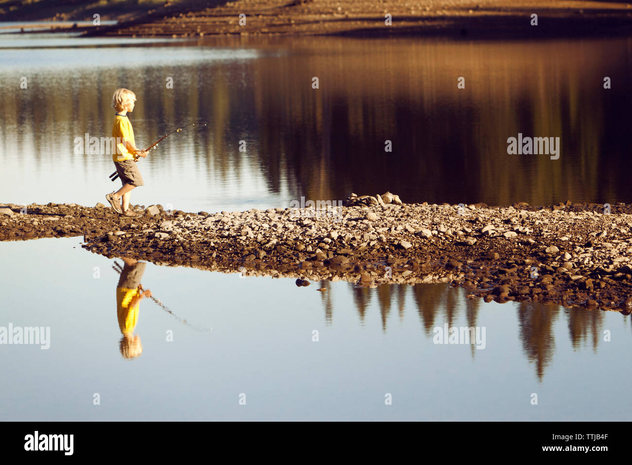 Side view of boy with fishing rod walking on rocks in lake Stock Photo ...