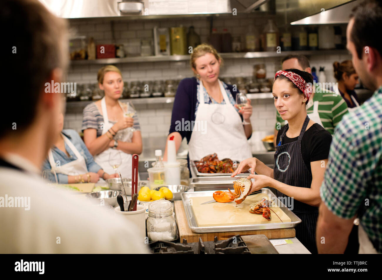 Female chef teaching students while standing at commercial kitchen ...