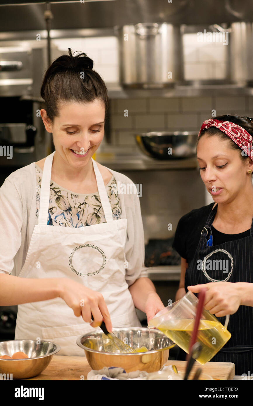 Happy women preparing food while standing by chef at commercial kitchen ...