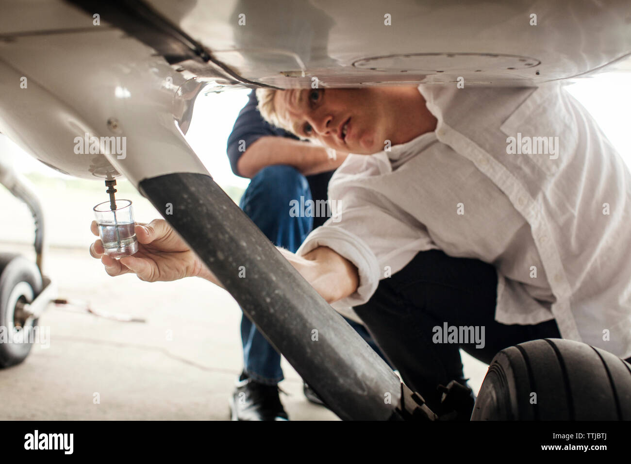 Mechanics repairing propeller airplane while crouching at airfield ...