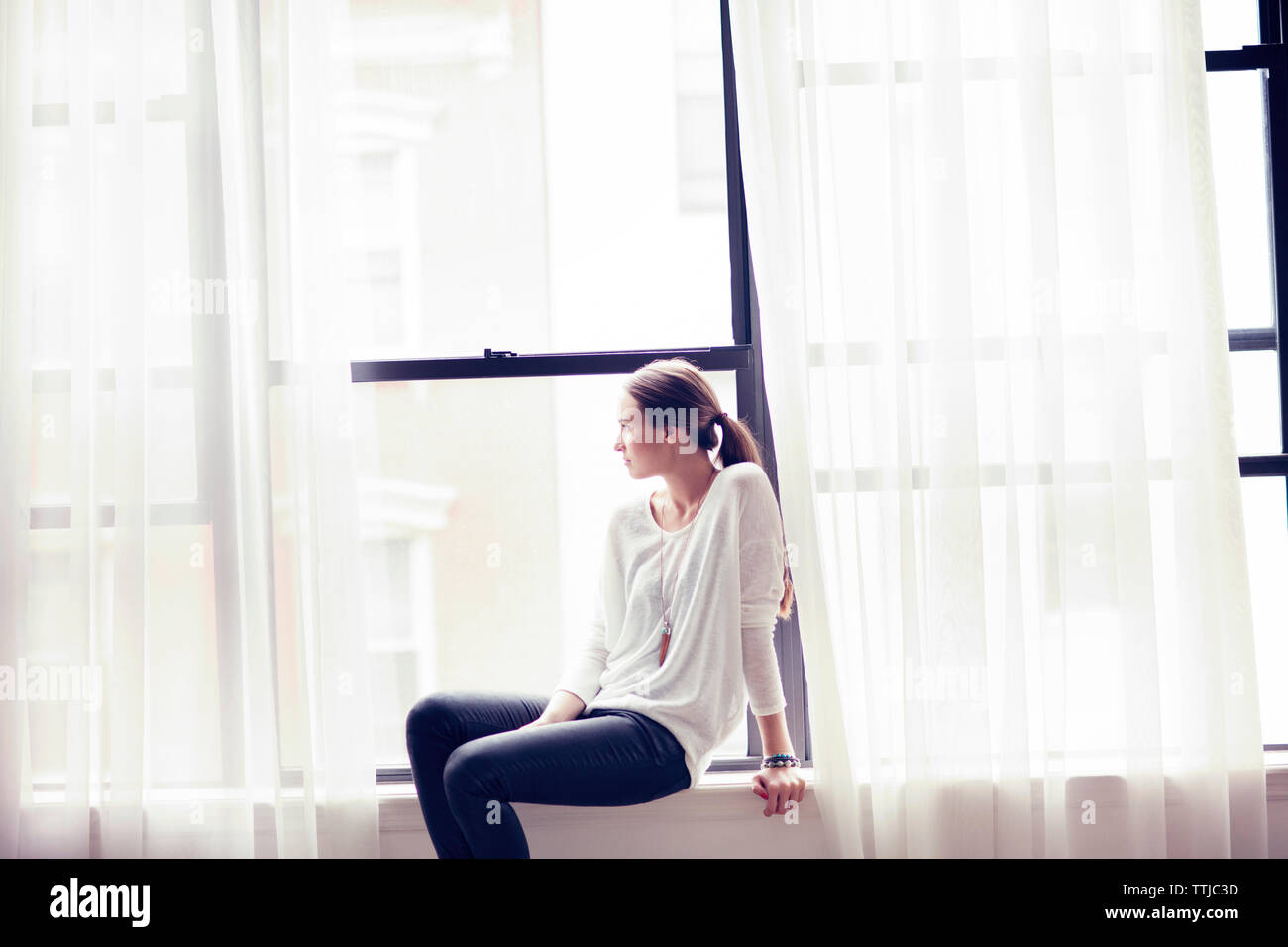 Woman looking through window at home Stock Photo - Alamy