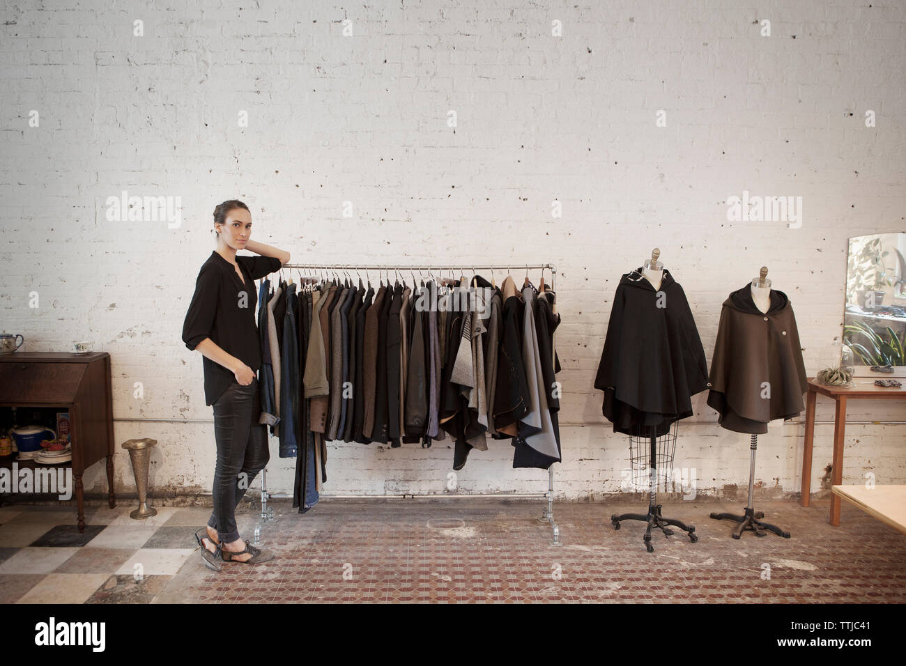 Portrait of woman leaning on clothes rack at clothing store Stock Photo ...