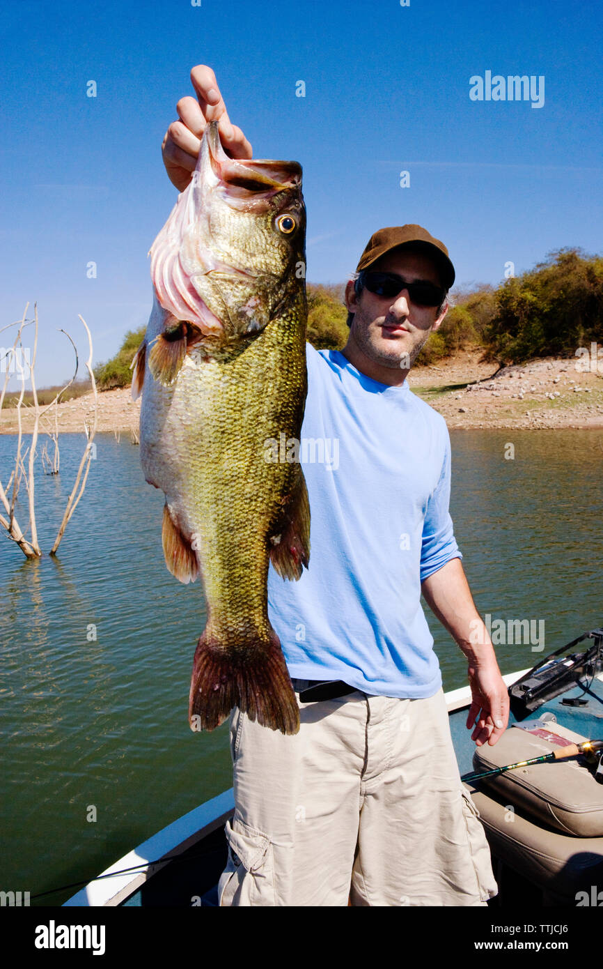 Portrait of man holding fish while standing in boat against clear sky ...