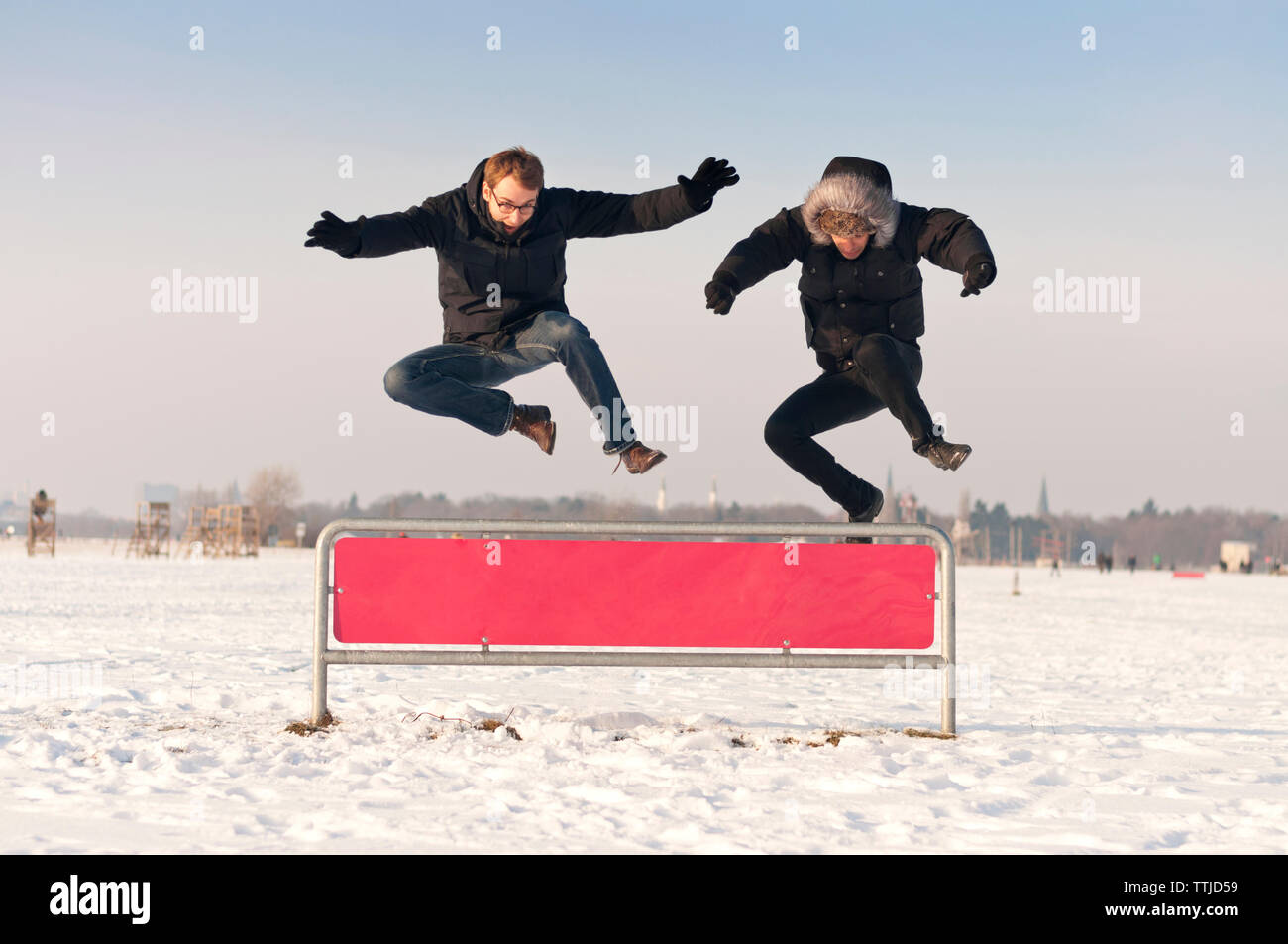 Happy friends jumping over hurdle at snow covered field Stock Photo - Alamy