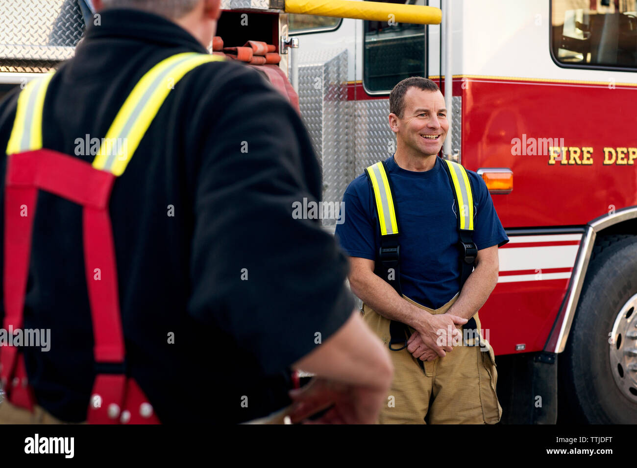 Happy fireman standing by coworker against fire engine Stock Photo - Alamy