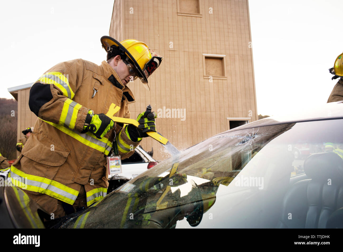 Firefighter cutting car windshield while standing against house Stock ...
