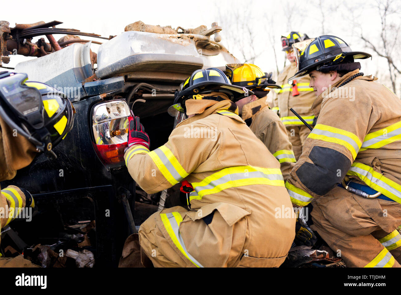 Firefighters crouching while lifting car Stock Photo - Alamy