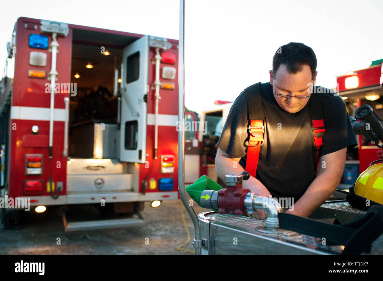 Firefighter fixing fire hose while standing against clear sky Stock ...