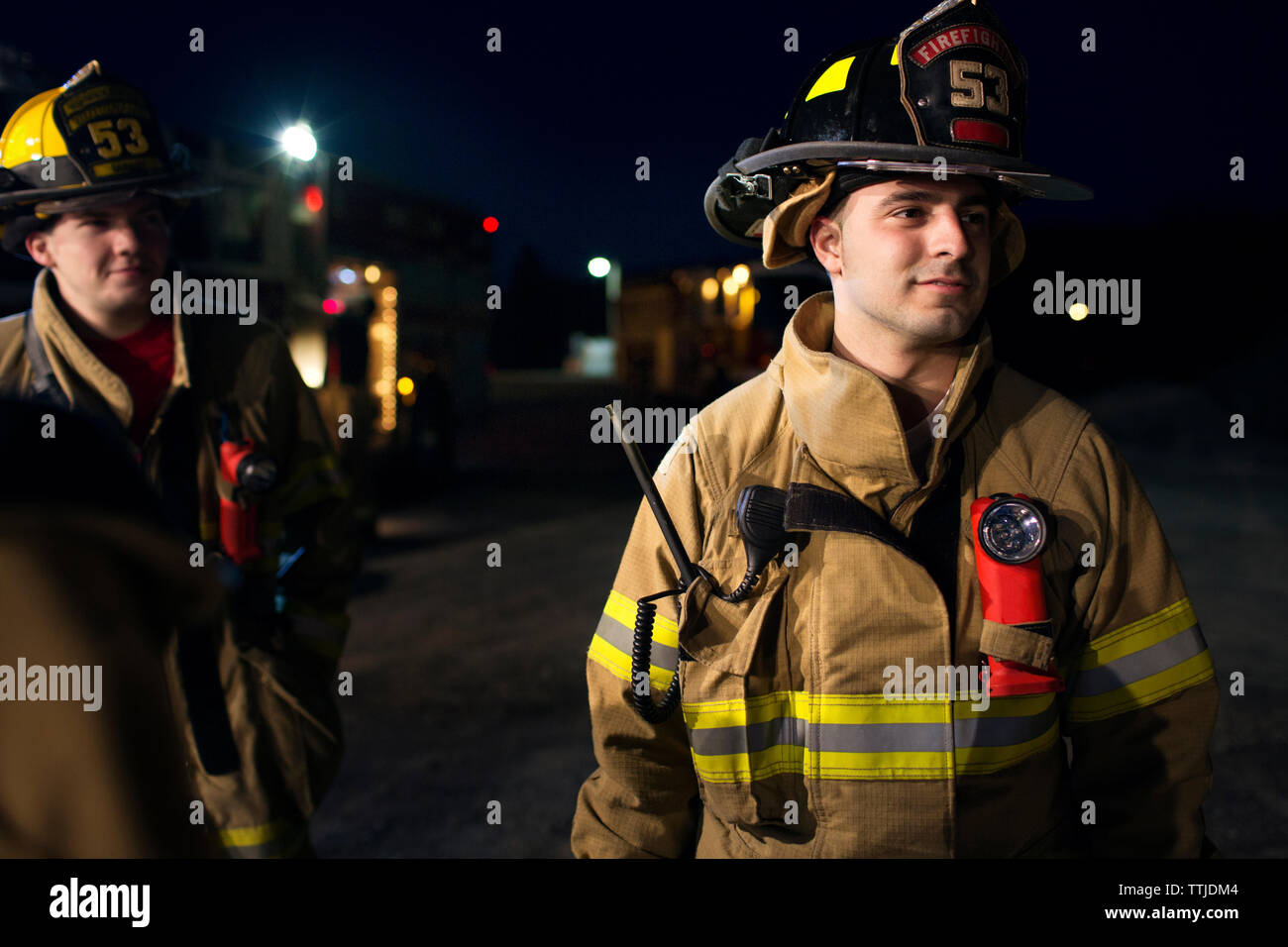 Firefighter looking away while standing by coworker at night Stock ...