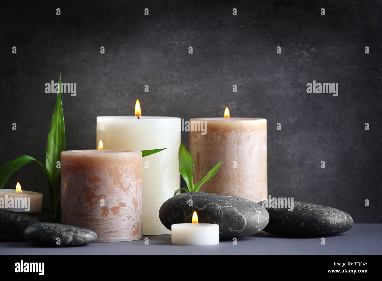 Composition of spa pebbles, candles and bamboo leaf on grey background ...