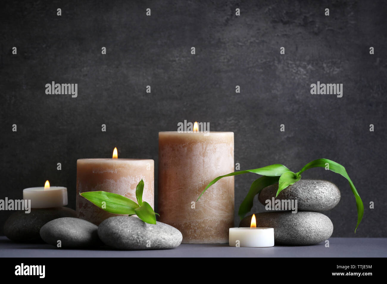 Composition of spa pebbles, candles and bamboo leaf on grey background ...