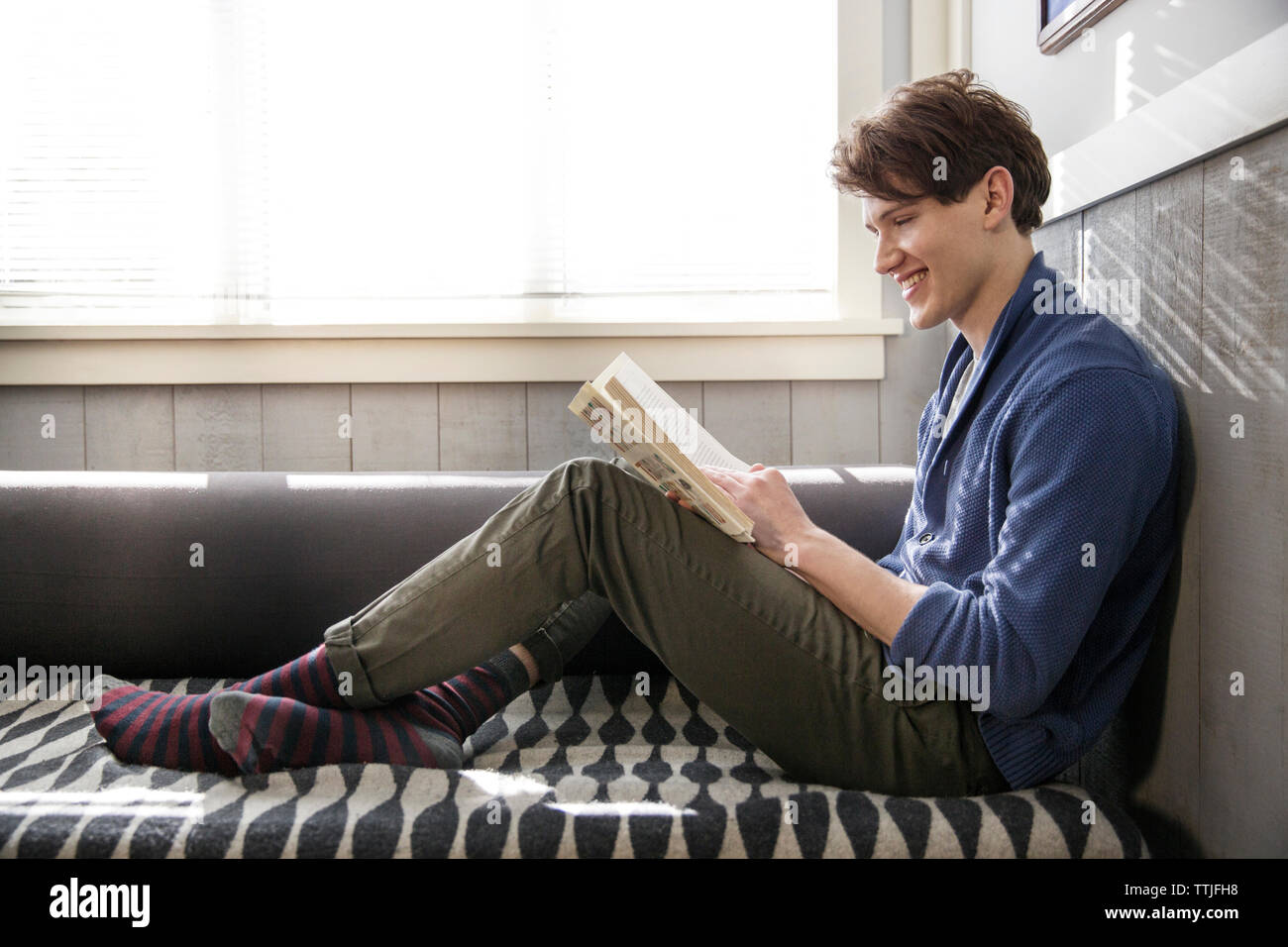 Side view of man smiling while reading book at home Stock Photo - Alamy