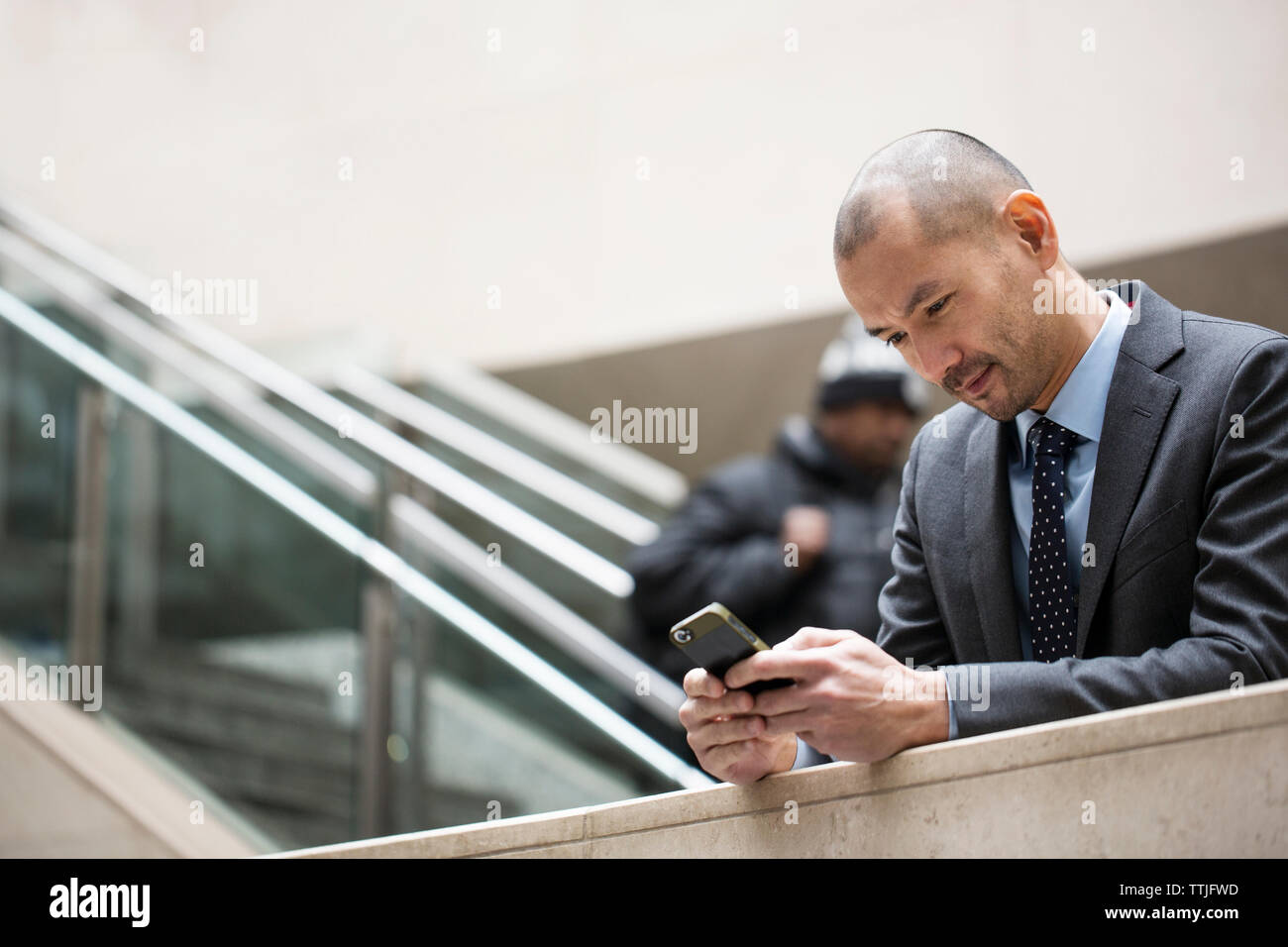 Man using mobile phone while leaning on railing at railroad station ...