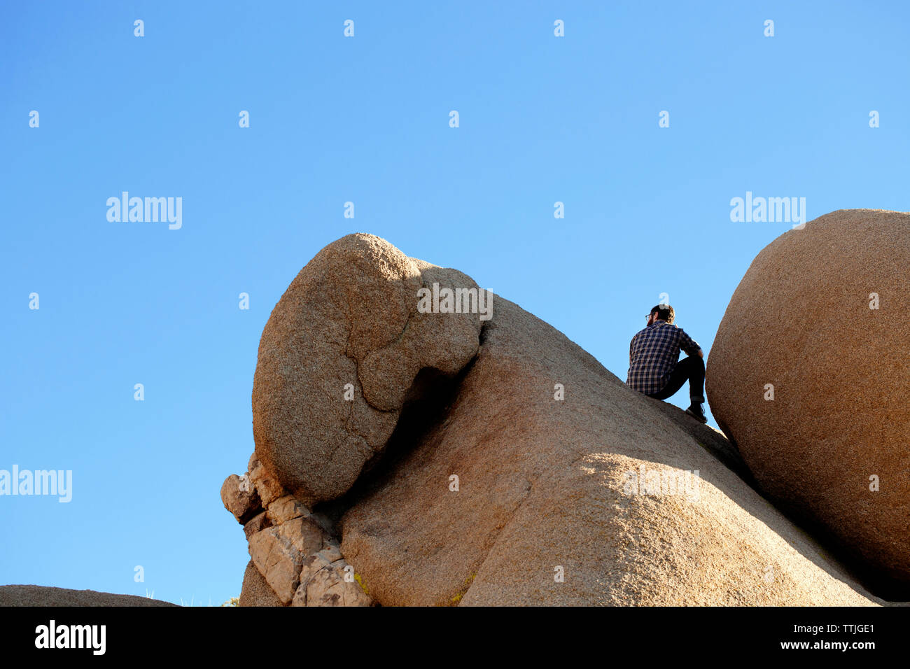 Rear view of man sitting on rock Stock Photo - Alamy