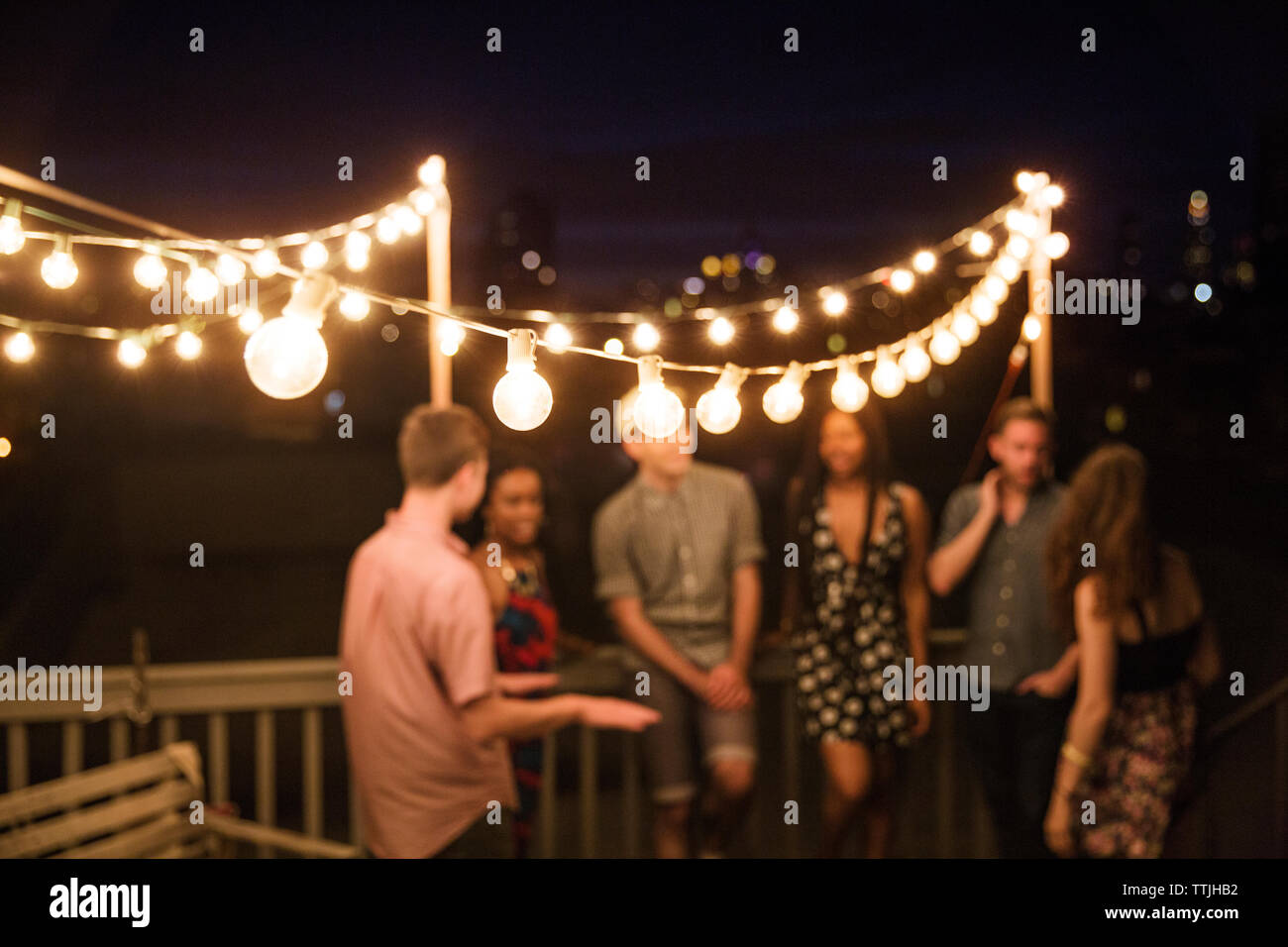 Friends talking while standing by railing on building terrace at night ...