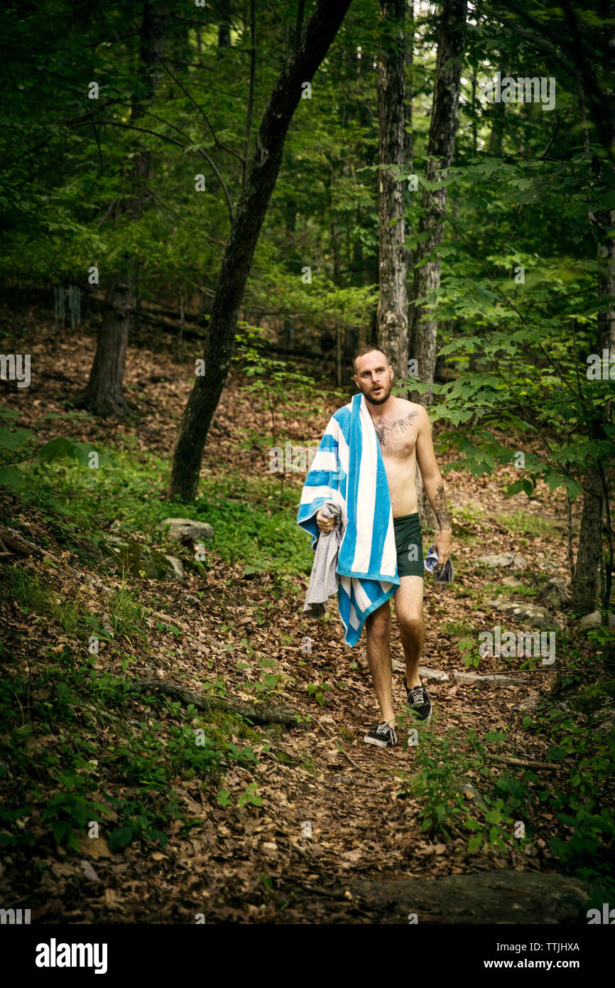 Shirtless man carrying towel and clothes while walking in forest Stock ...