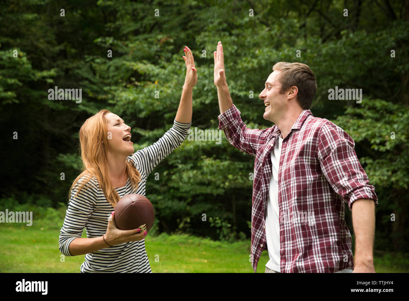 Couple high fiving while playing football in lawn Stock Photo - Alamy