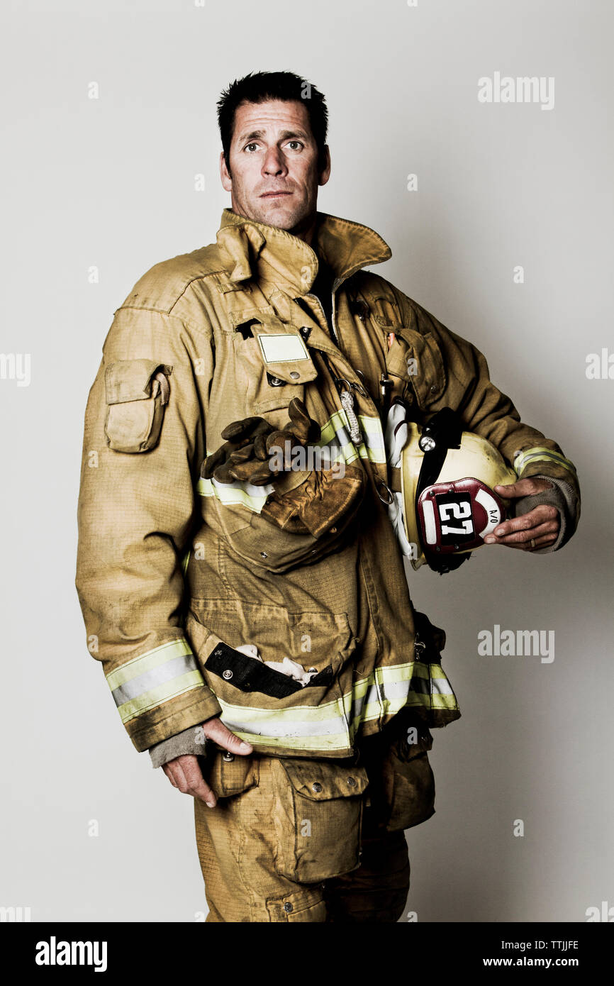 Portrait of firefighter holding helmet standing against white ...