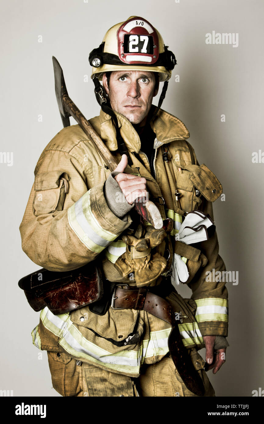 Portrait of firefighter holding shovel standing against white ...