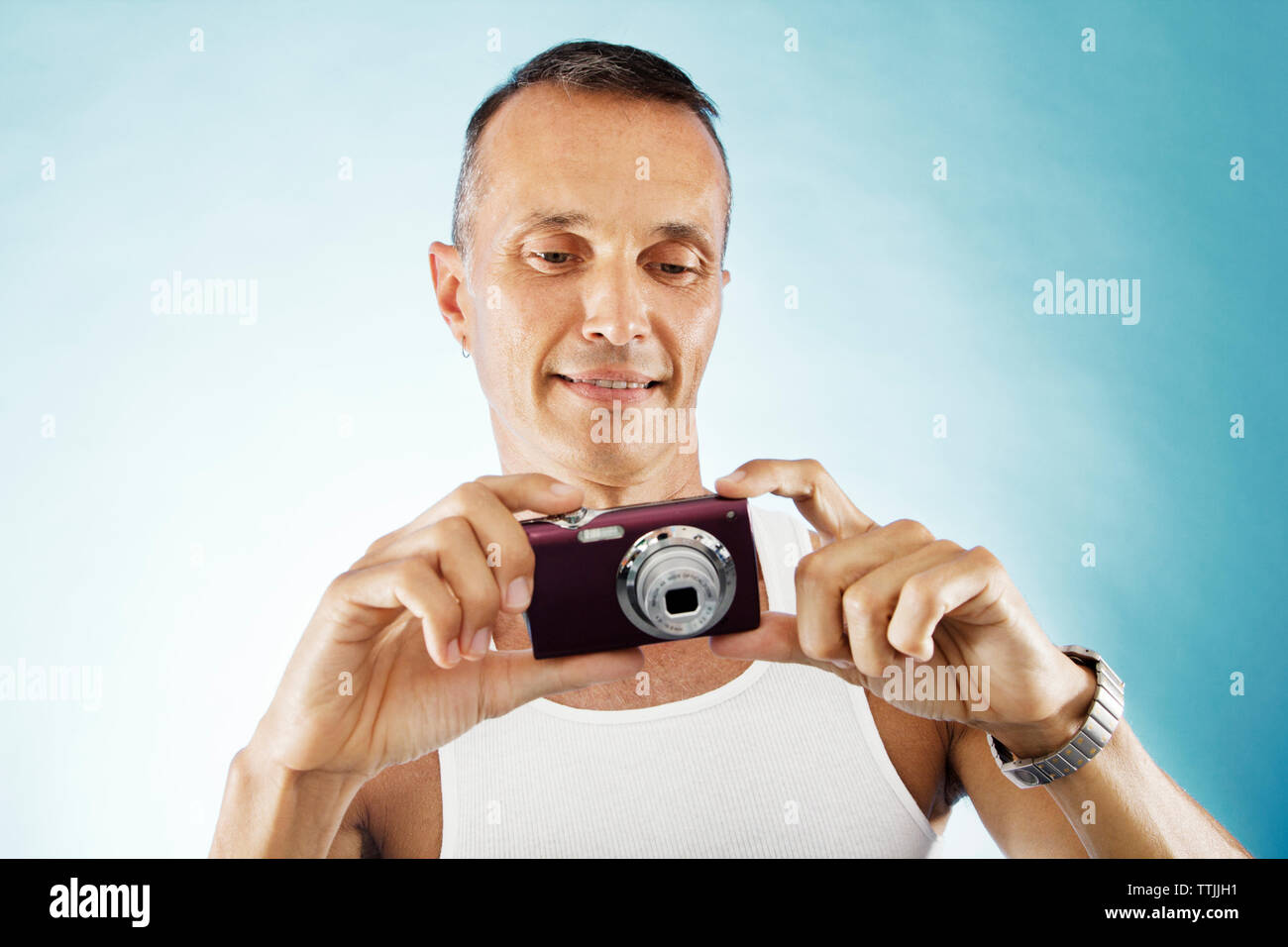 Happy man holding camera against blue background Stock Photo - Alamy