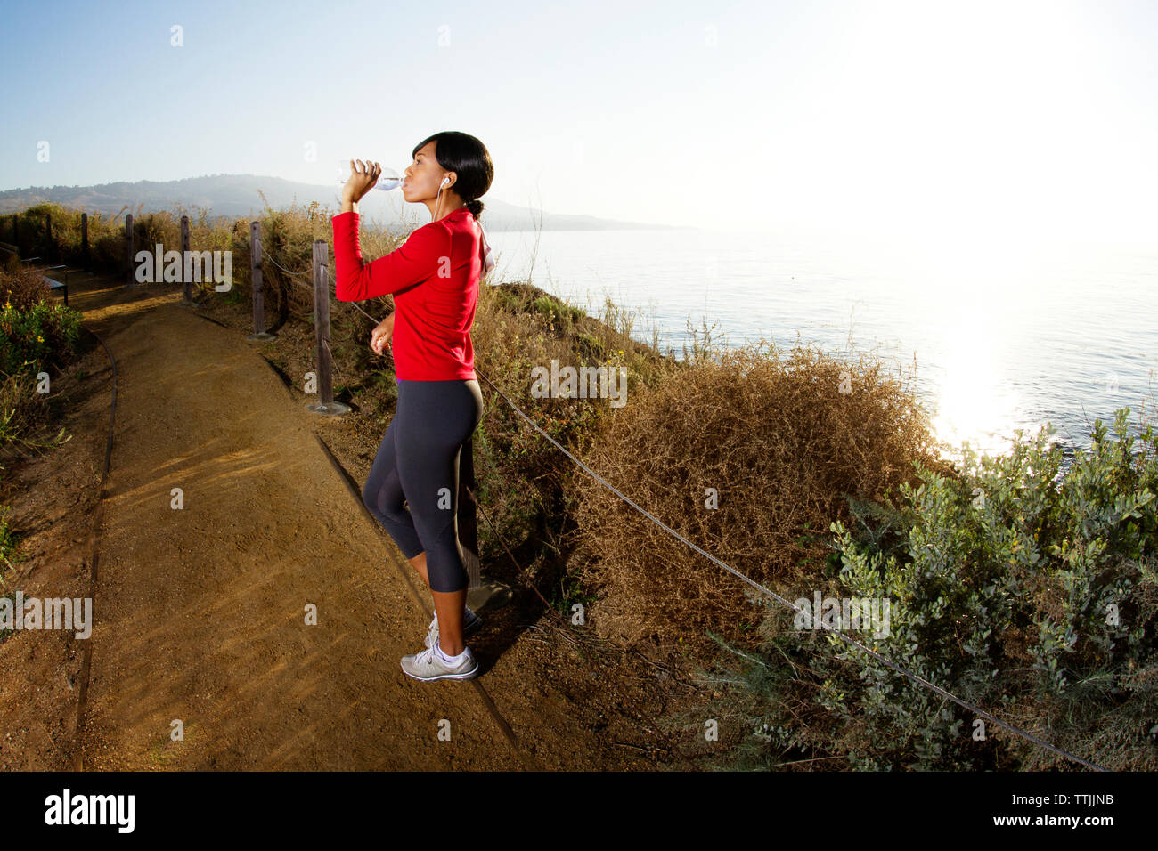 Woman drinking water while standing on road against sea Stock Photo - Alamy