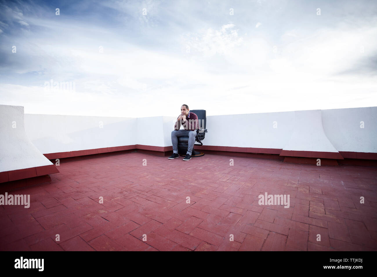 Thoughtful man sitting on chair at building terrace Stock Photo - Alamy