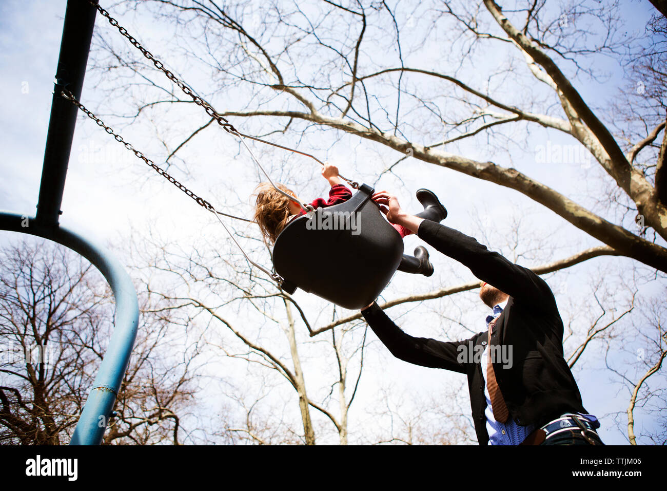 Low angle view of father swinging daughter at playground Stock Photo ...