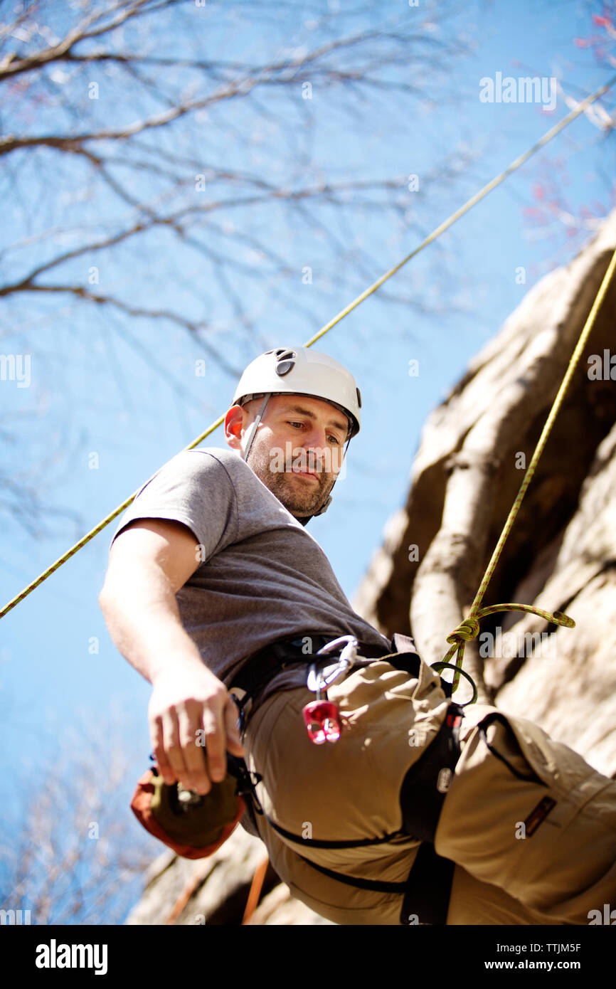 Side view of man rappelling on rock face Stock Photo - Alamy