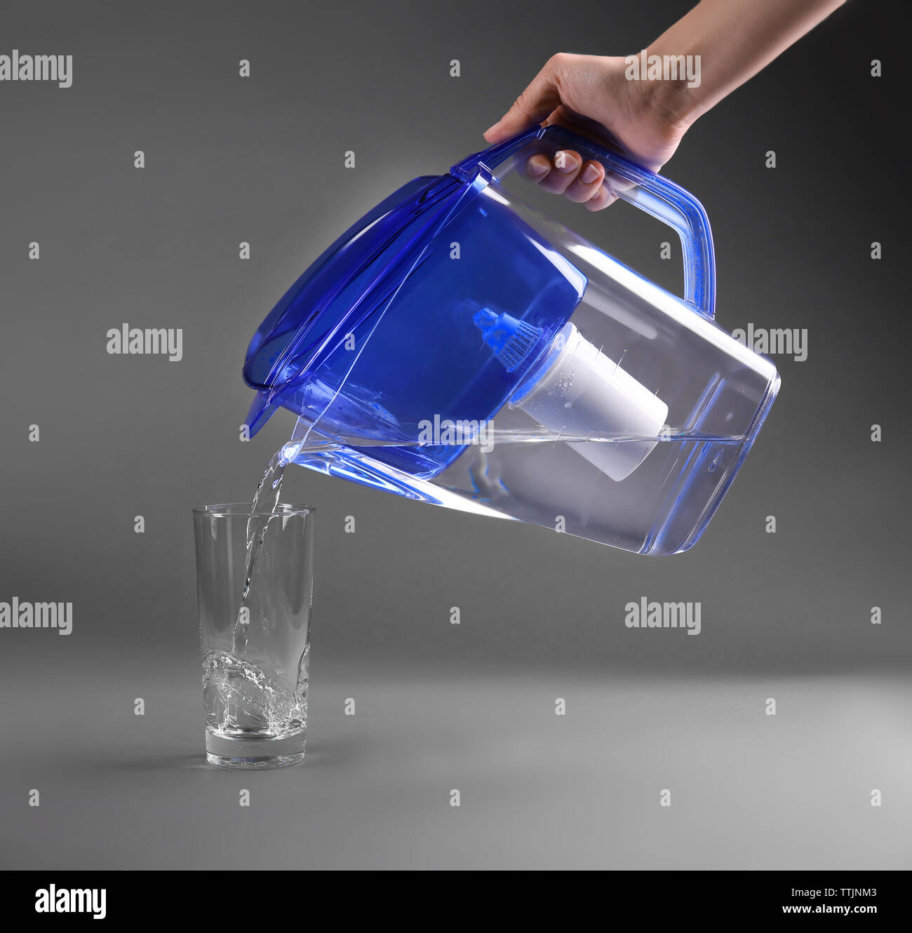 Female hand pouring water into glass on grey background Stock Photo - Alamy