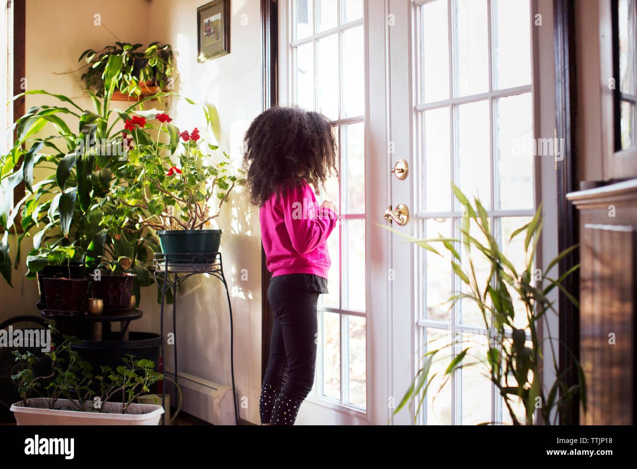 Side view of girl looking through glass door at home Stock Photo - Alamy