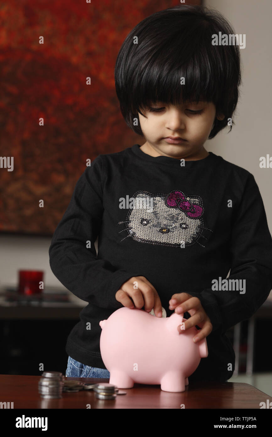 Indian girl putting a coin into a piggy bank Stock Photo - Alamy