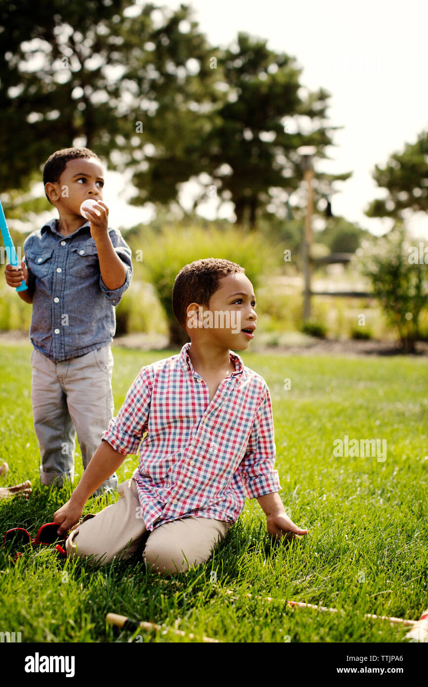 Brothers looking away while relaxing in backyard Stock Photo - Alamy