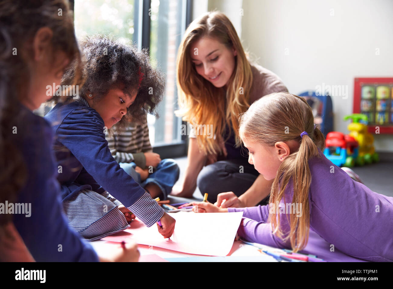 Teacher and students drawing on papers at child care Stock Photo - Alamy