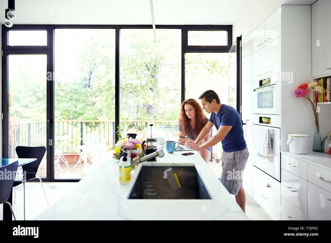 Couple using laptop computer while standing at kitchen counter by ...