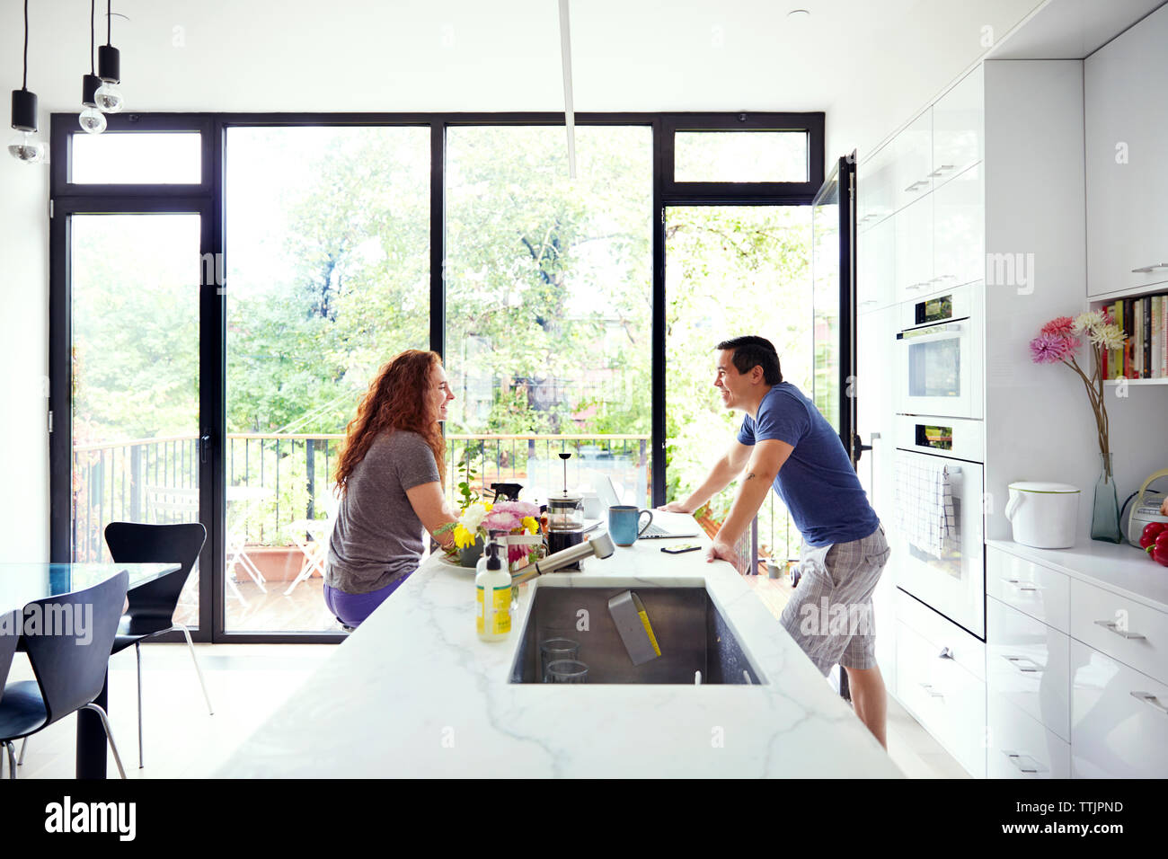 Happy couple talking at kitchen counter by window Stock Photo - Alamy