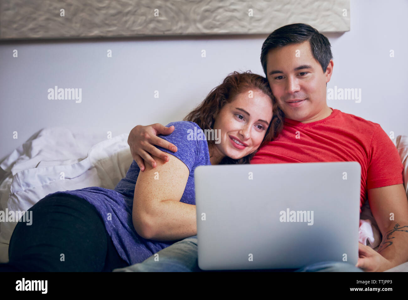 Loving couple looking at laptop computer while lying on bed at home ...