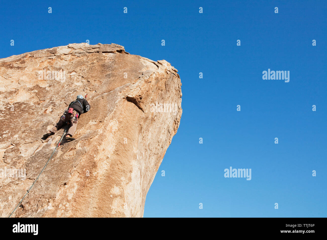 Low angle view of man rock climbing against clear blue sky Stock Photo ...