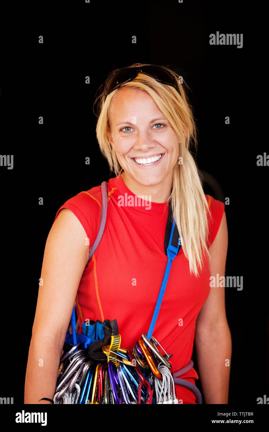 Portrait of smiling rock climber with various hooks standing against ...
