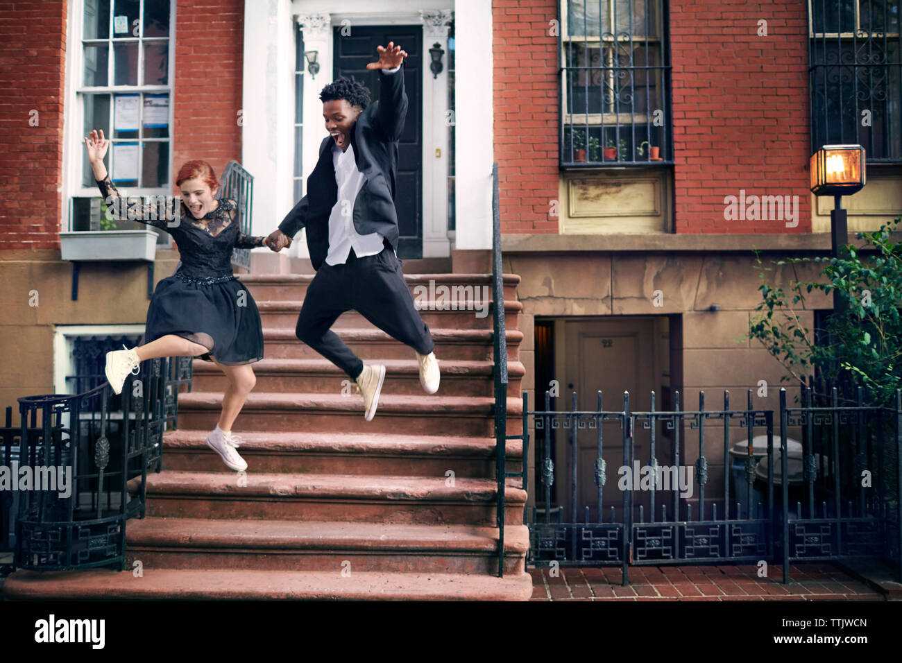 Cheerful couple jumping against house Stock Photo - Alamy