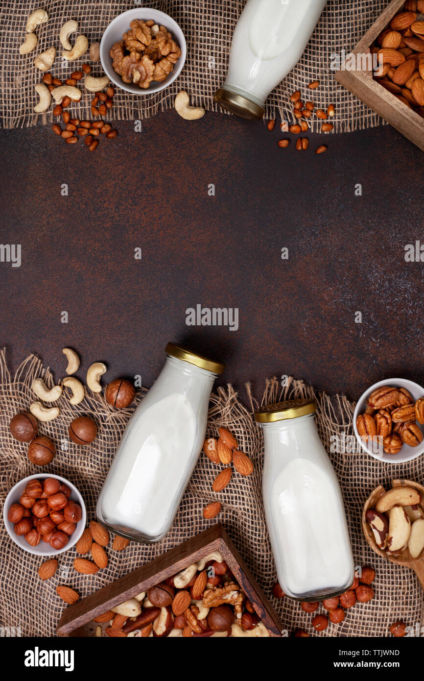 vegetable nut milk in glass bottles, different types of nuts on a dark ...