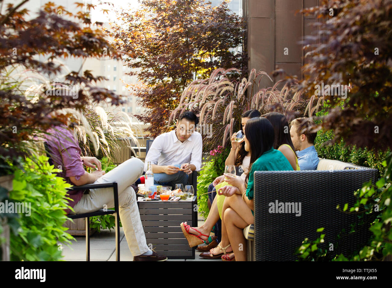 Friends enjoying food while sitting at building terrace Stock Photo - Alamy
