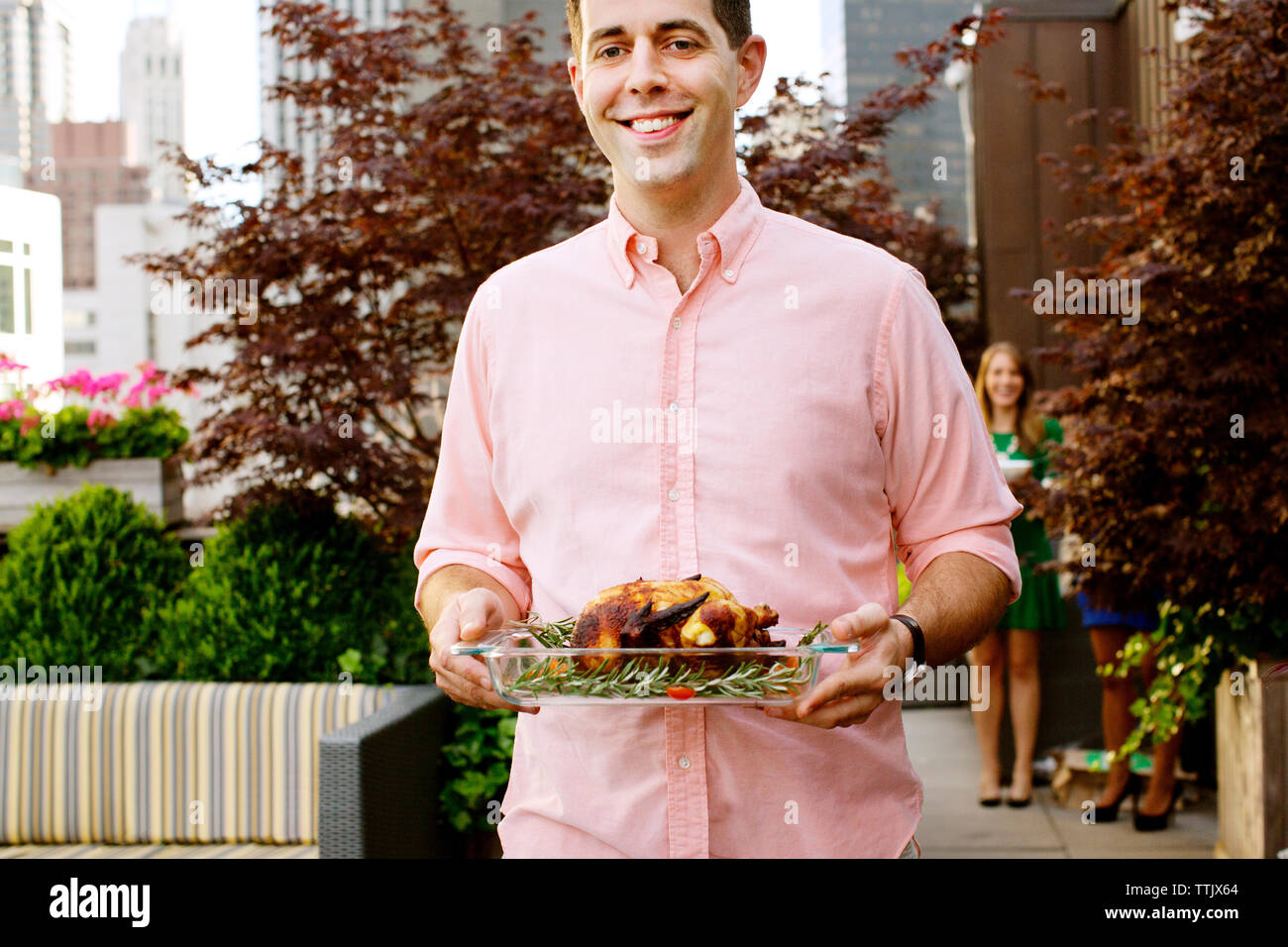 Midsection of smiling man carrying roasted chicken in tray while ...