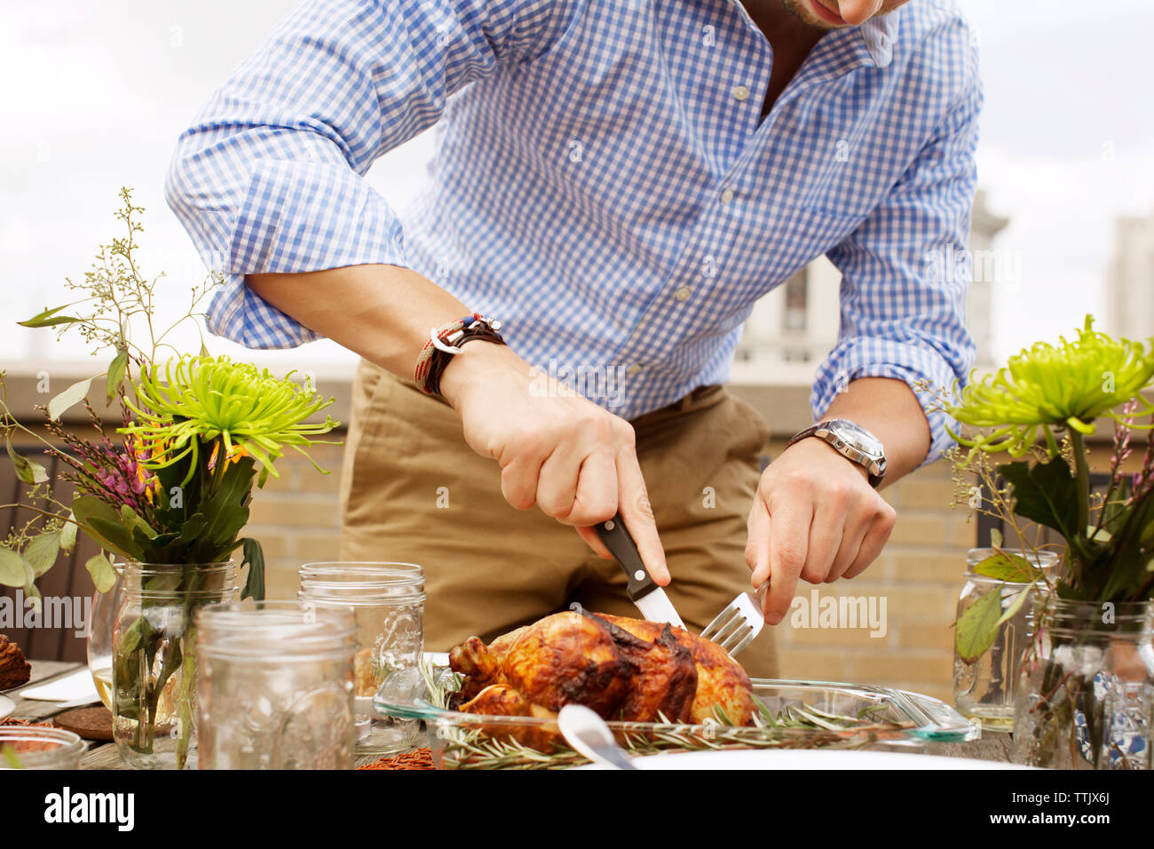 Midsection of man carving roasted chicken at table on building terrace ...