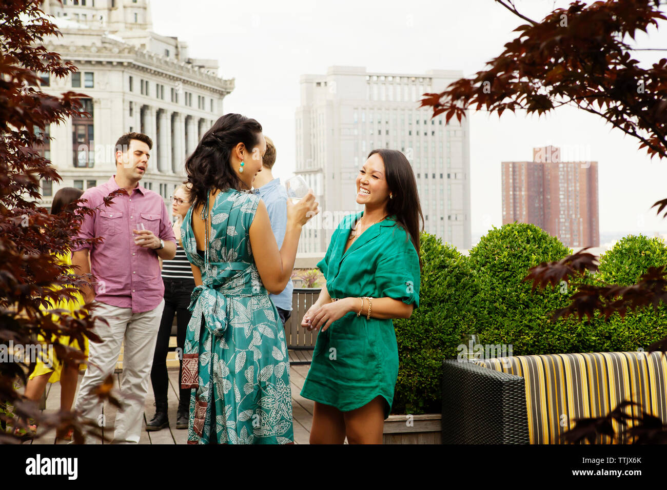 Happy friends talking while standing by sofa on building terrace Stock ...