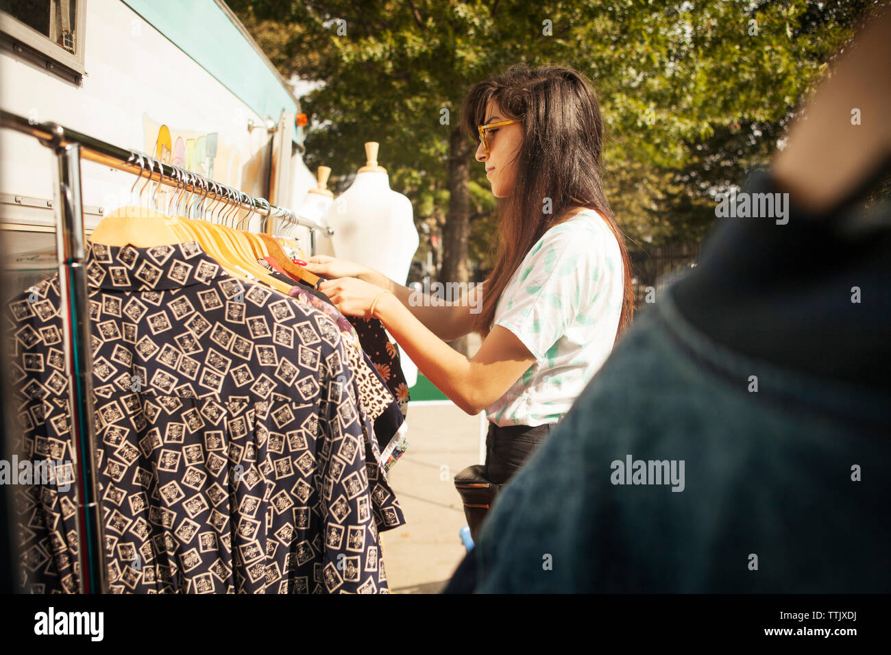 Side view of woman looking at clothing in rack Stock Photo - Alamy