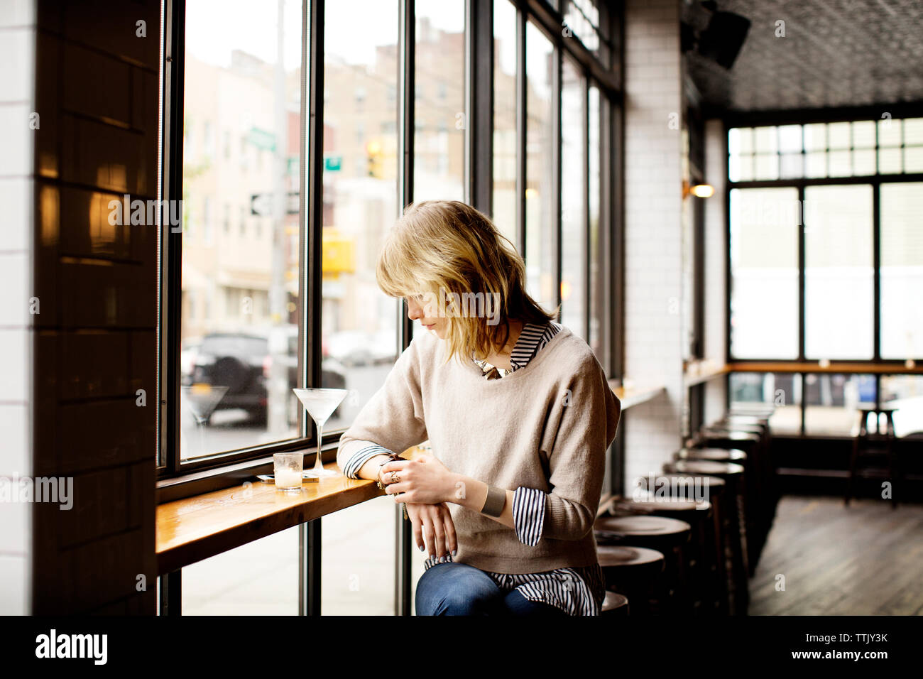 Woman looking down while sitting in bar Stock Photo - Alamy